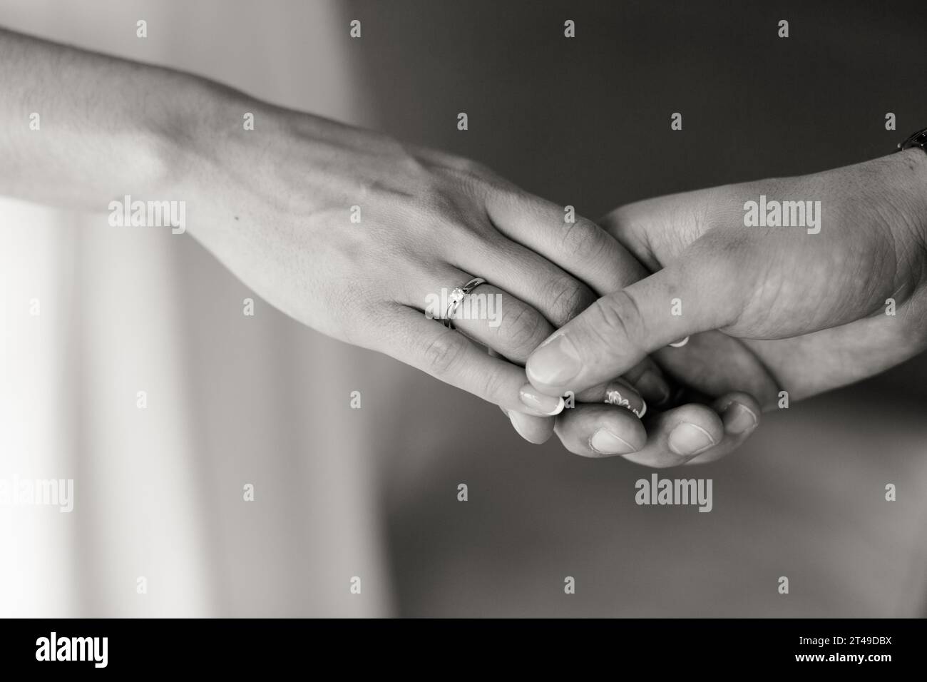 Close-up monochrome shot of hands intertwined with an engagement ring ...