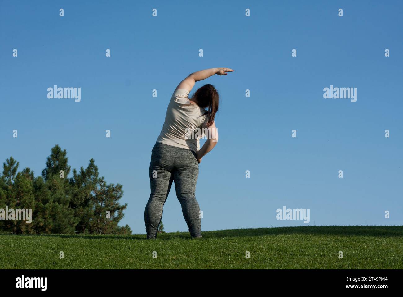 overweight middle-aged woman does exercises in park standing on grass ...