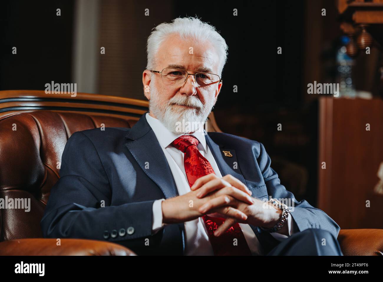 A confident and successful university rector in his 60s or 70s, sitting ...