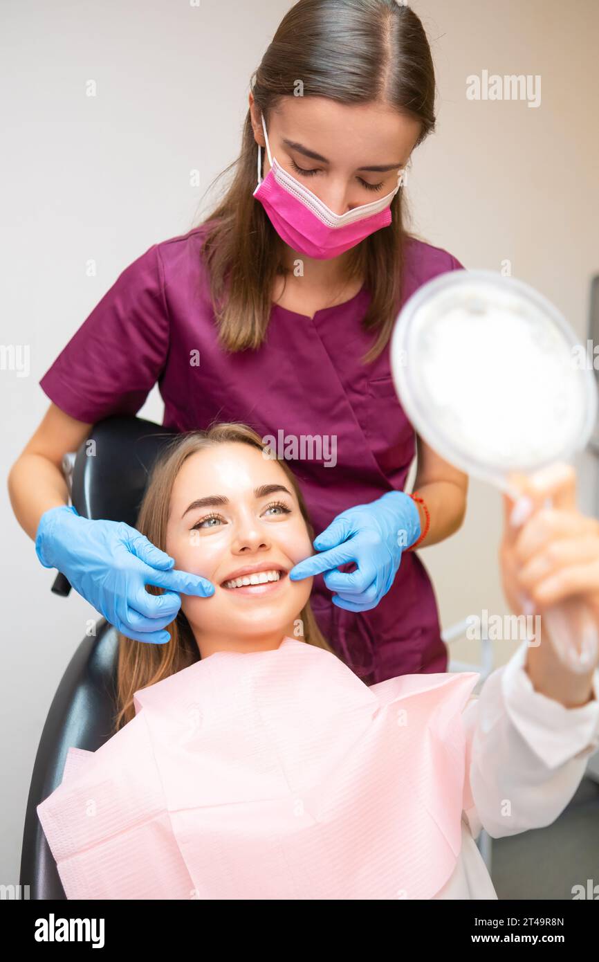 Young patient is looking in the mirror and admires her perfect smile ...