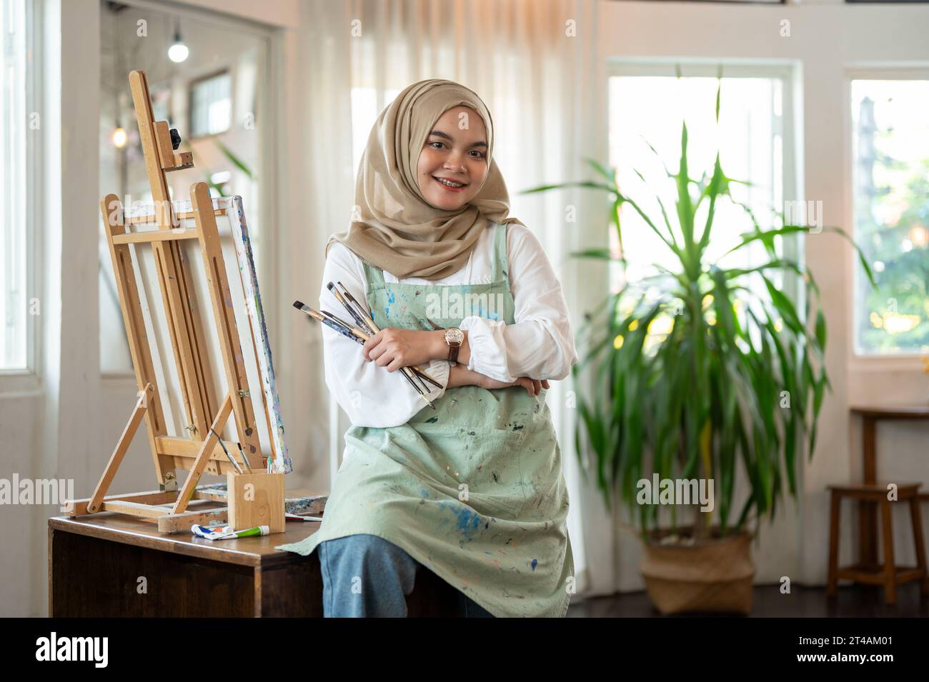 A charming and creative young Asian-Muslim female artist in an apron ...