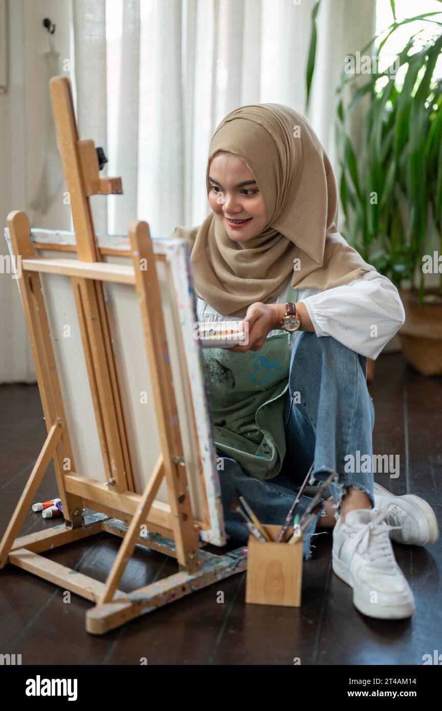 A beautiful and happy young Asian-Muslim female artist is sitting on ...