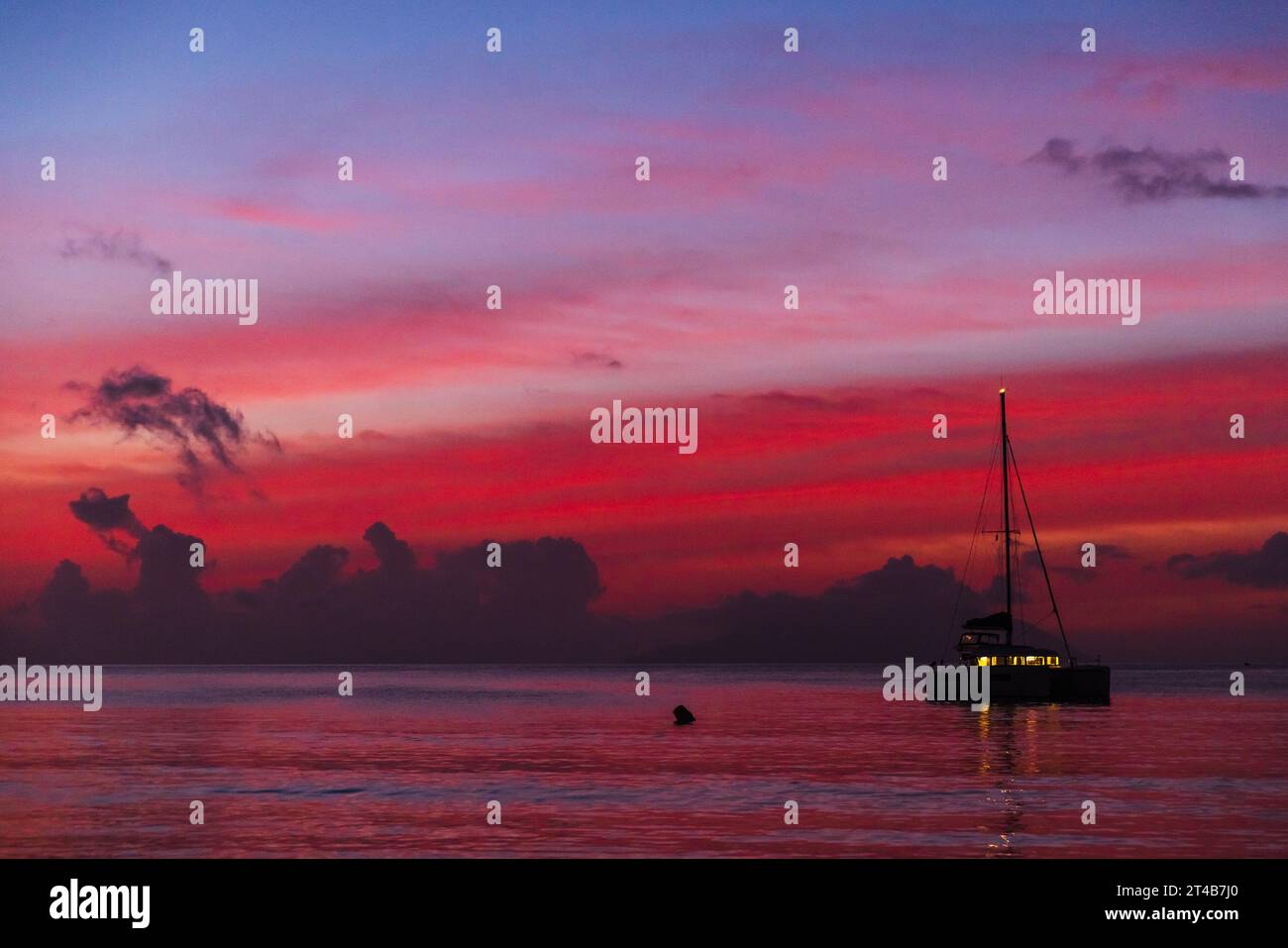 Coastal landscape with silhouette of catamaran yacht under red sky at ...