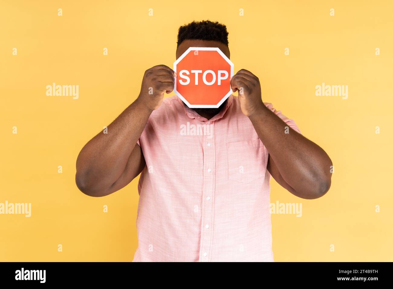 Portrait of man wearing pink shirt covering face with Stop symbol ...