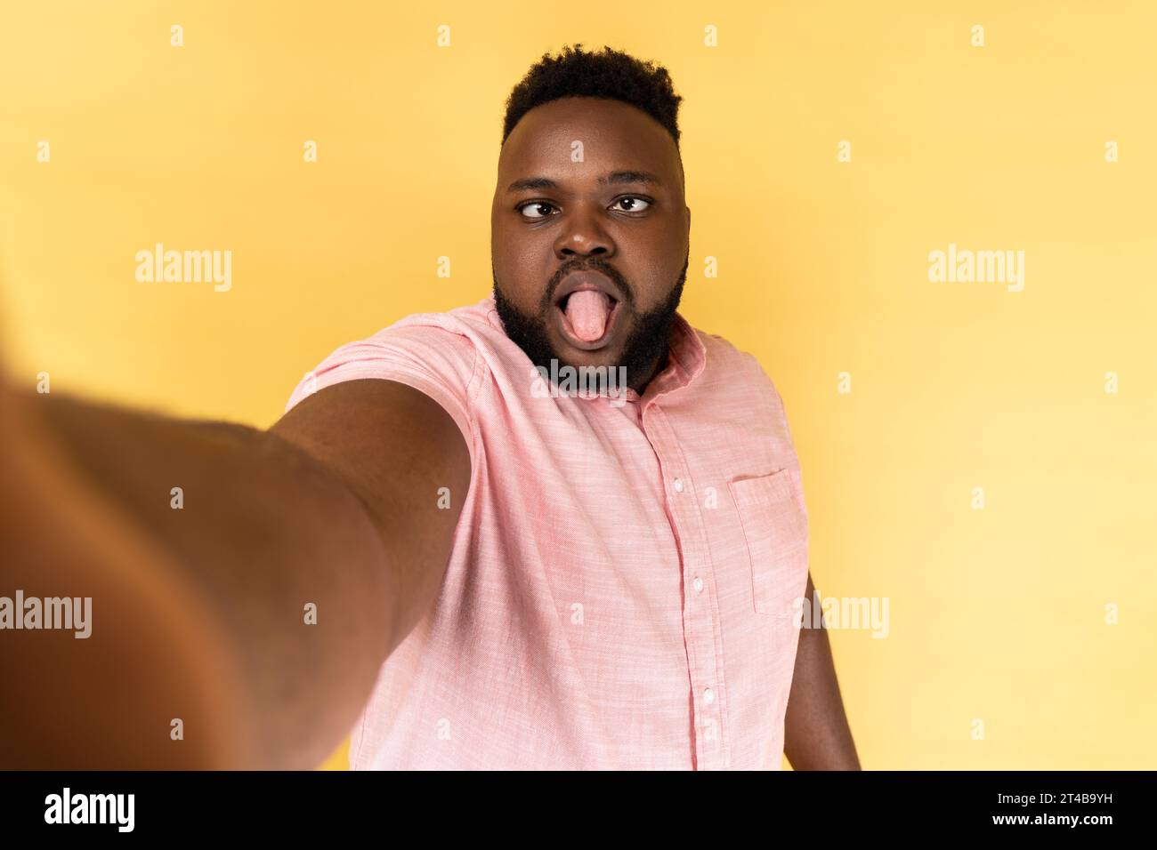 Portrait of funny childish bearded man wearing pink shirt making point ...