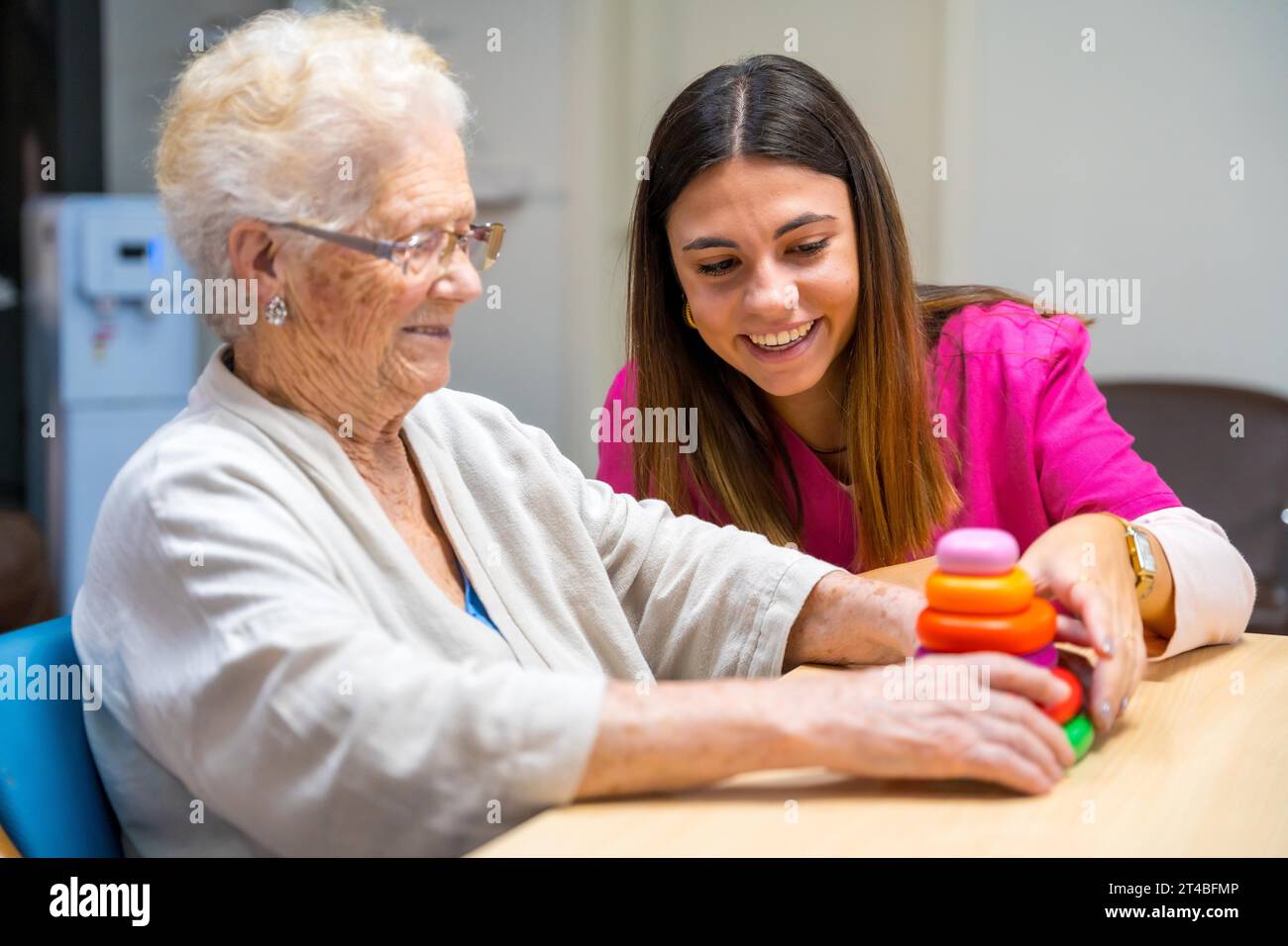 Cute nurse helping a woman to play board skill game in a nursing home ...
