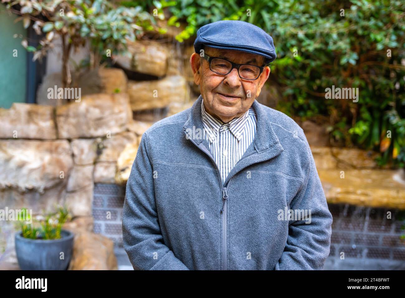 Portrait of a senior man with beret standing in a garden in a geriatric ...