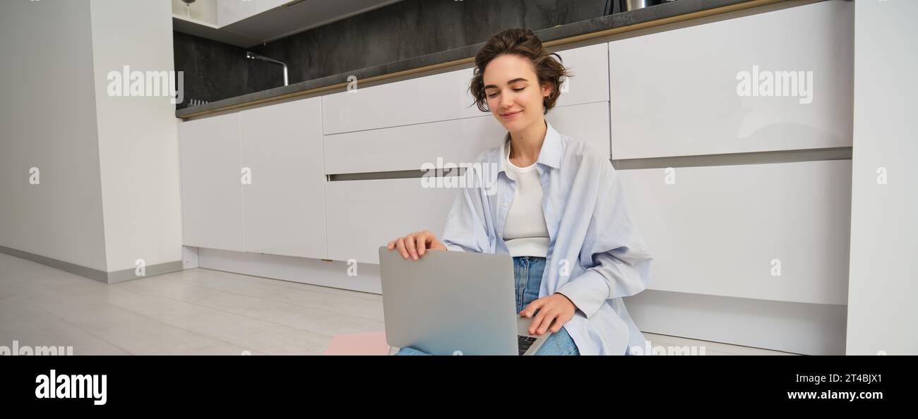 Young woman works from home on kitchen floor, does homework on laptop ...