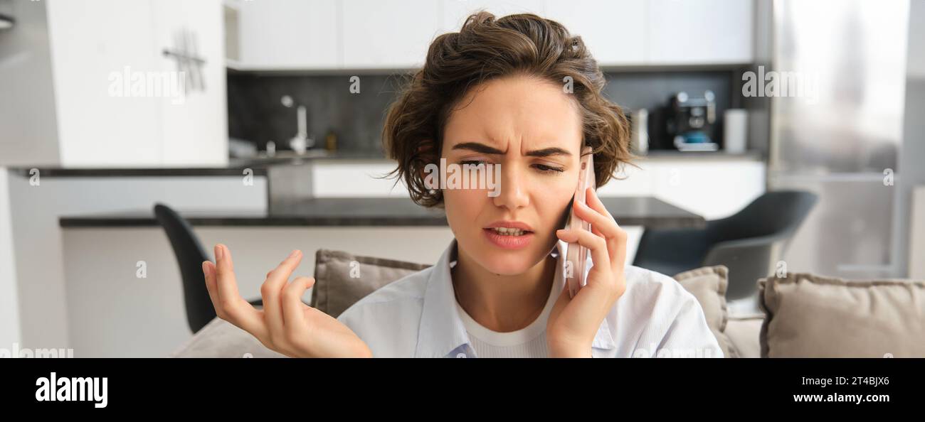 Close up portrait of confused young woman answers phone call and shrugs ...