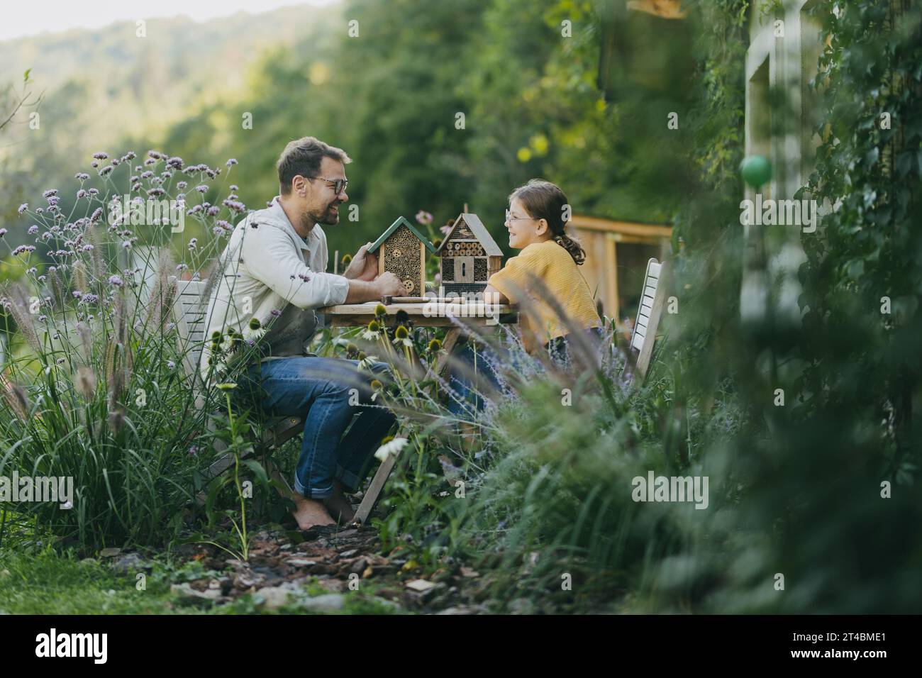 Father with daughter making bug hotel, or insect house outdoors in the ...