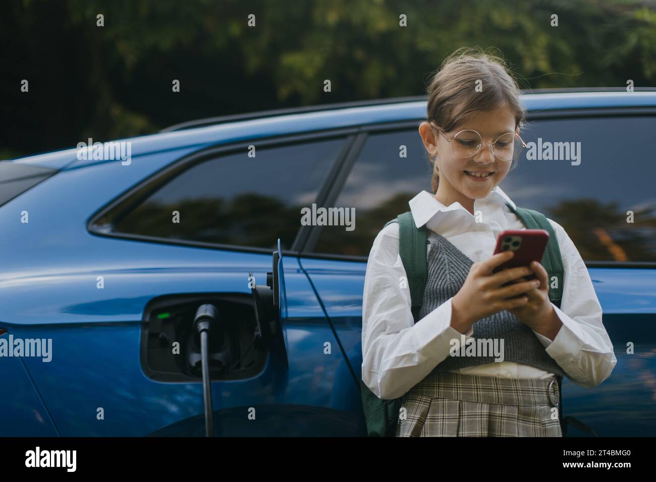 Girl and electric car with charger in charging port. Girl scrolling on ...