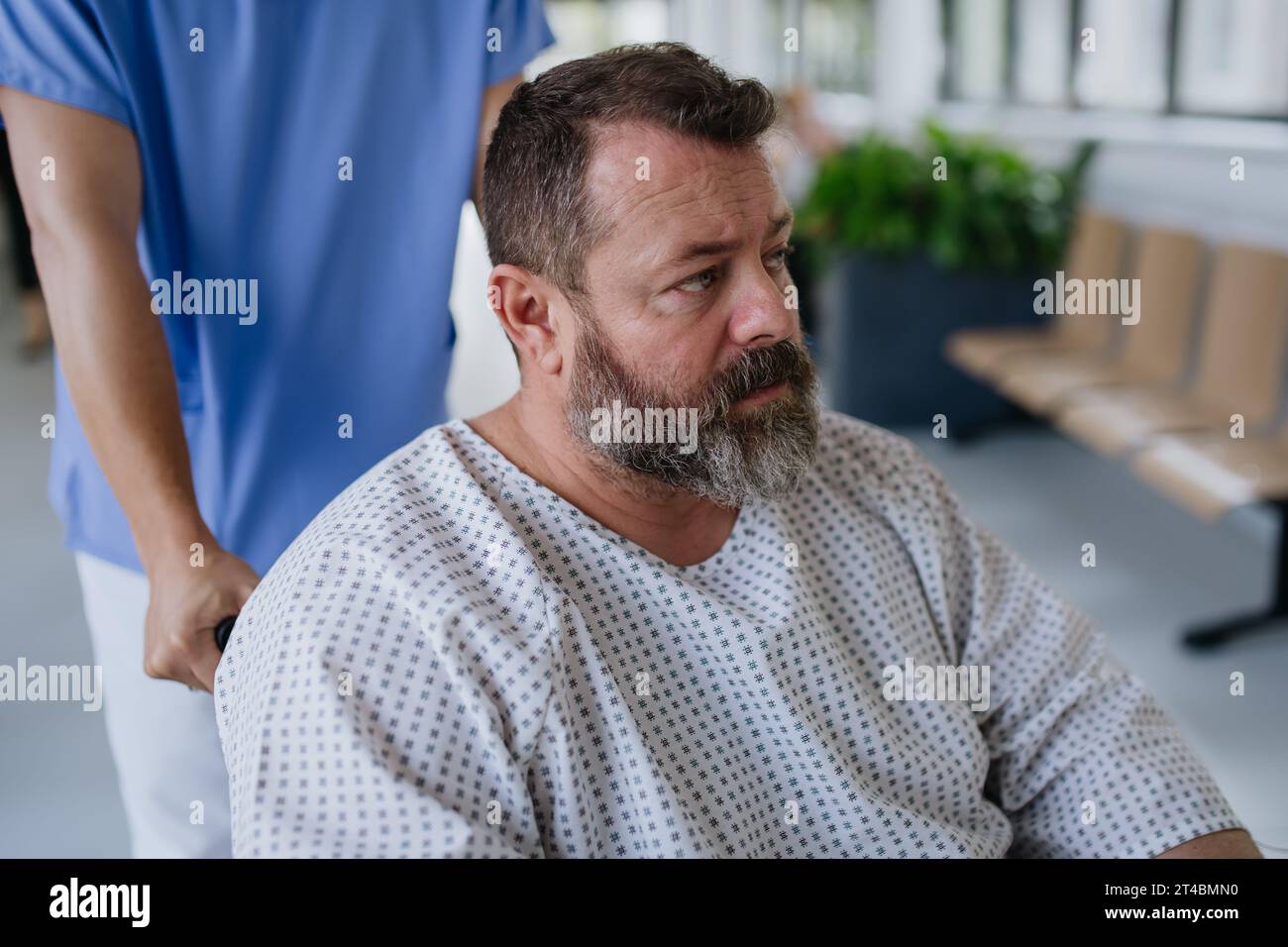 Male nurse pushing a patient in a wheelchair along a hospital corridor ...