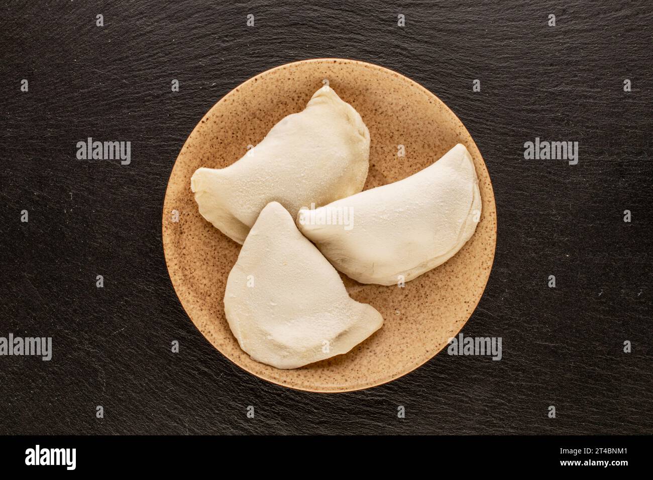 Three frozen semi-finished dumplings in a ceramic plate on slate stone ...