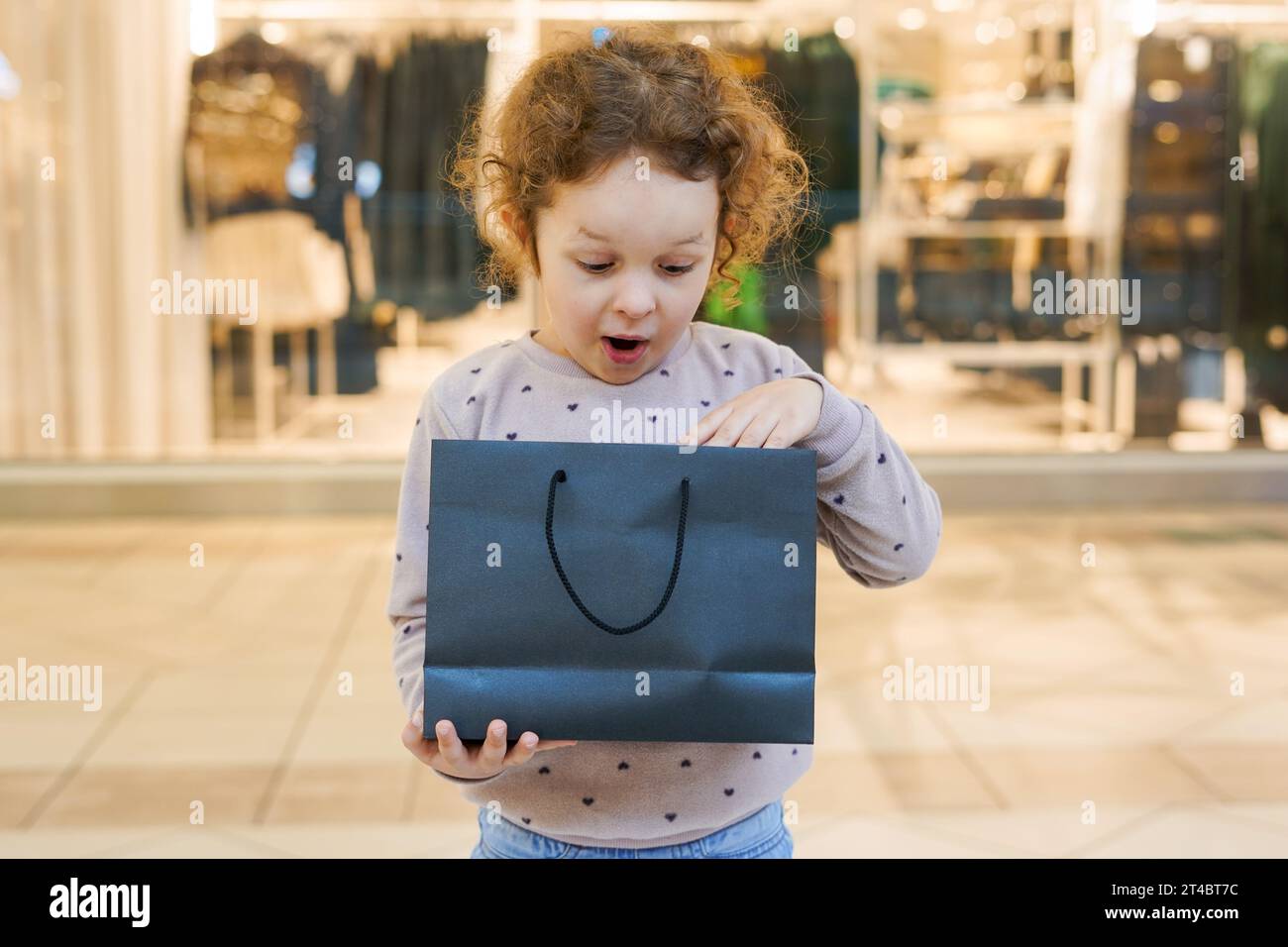 Surprised and happy child girl looking into shopping bag in cloth store ...