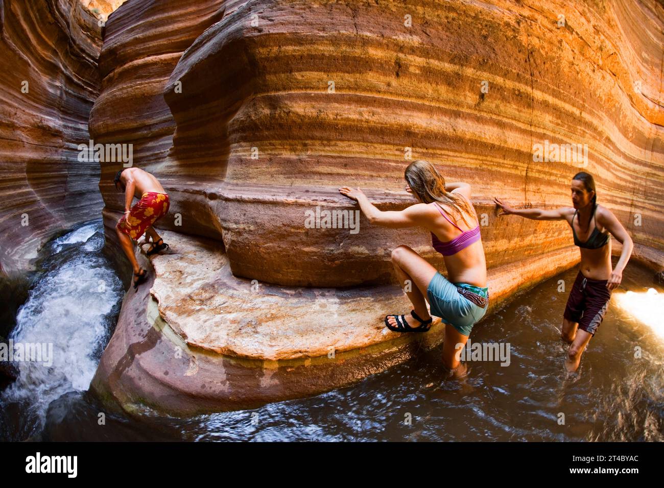 Three people scrambling down a slot canyon with flowing water, Deer ...