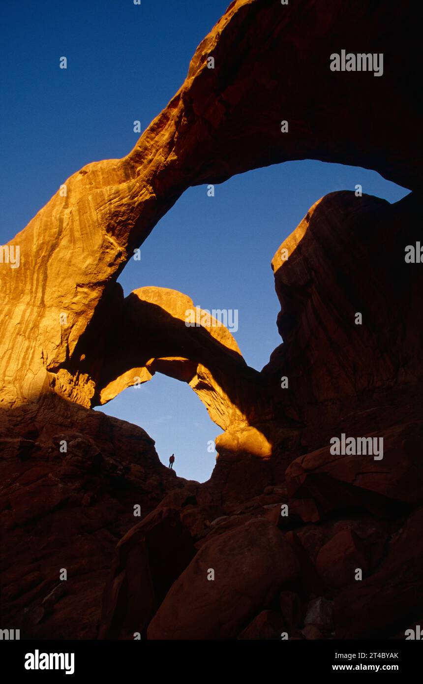 A man beneath double arch, Arches National Park, Moab, Utah Stock Photo ...