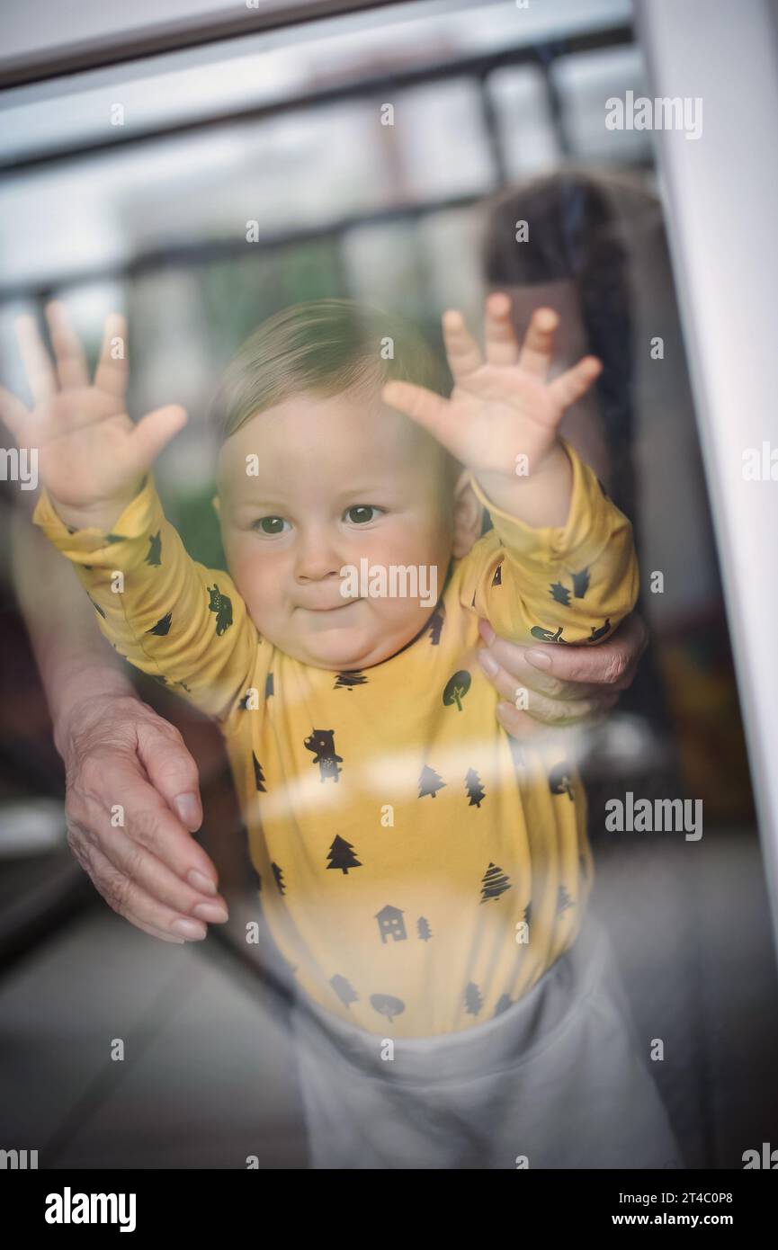 Portrait of cute smiling baby boy looks through the window. Joy and ...