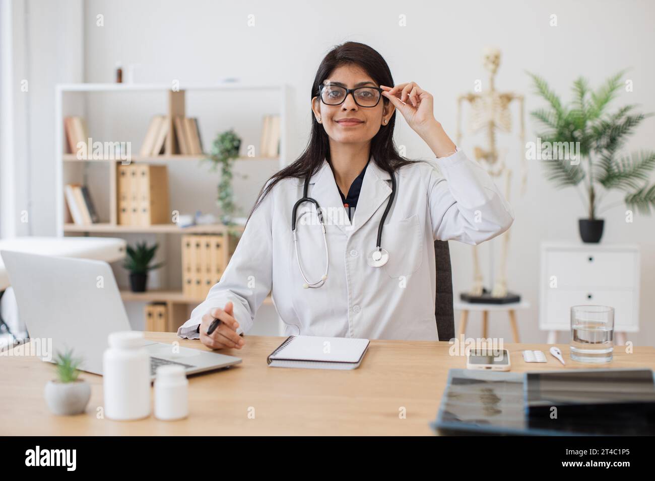 Female general practitioner in medical gown sitting and keeping hand on ...