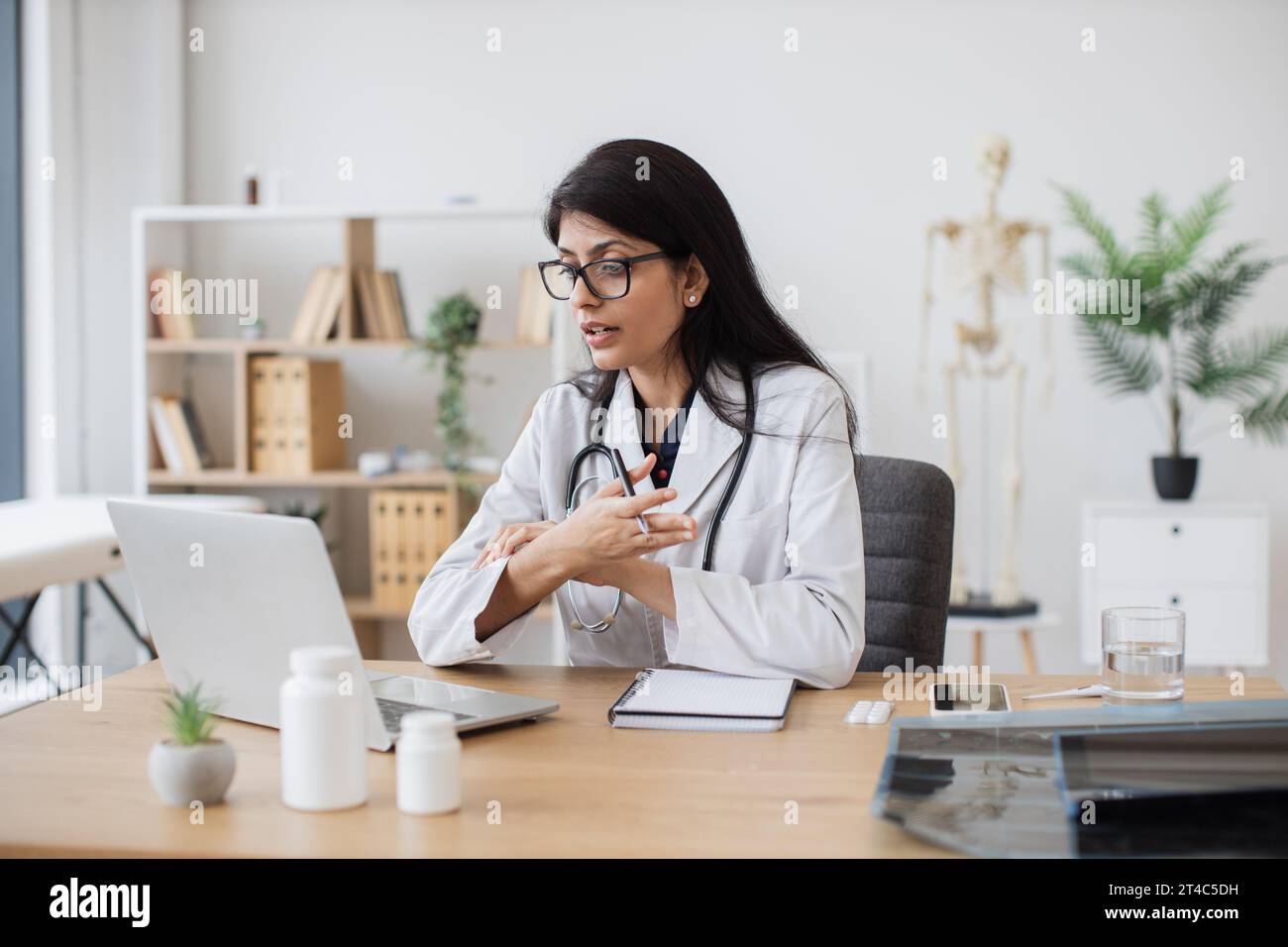Focused female doctor with stethoscope having video conference on ...