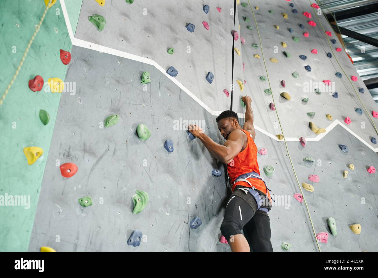 sporty young african american man using safety rope and harness to ...