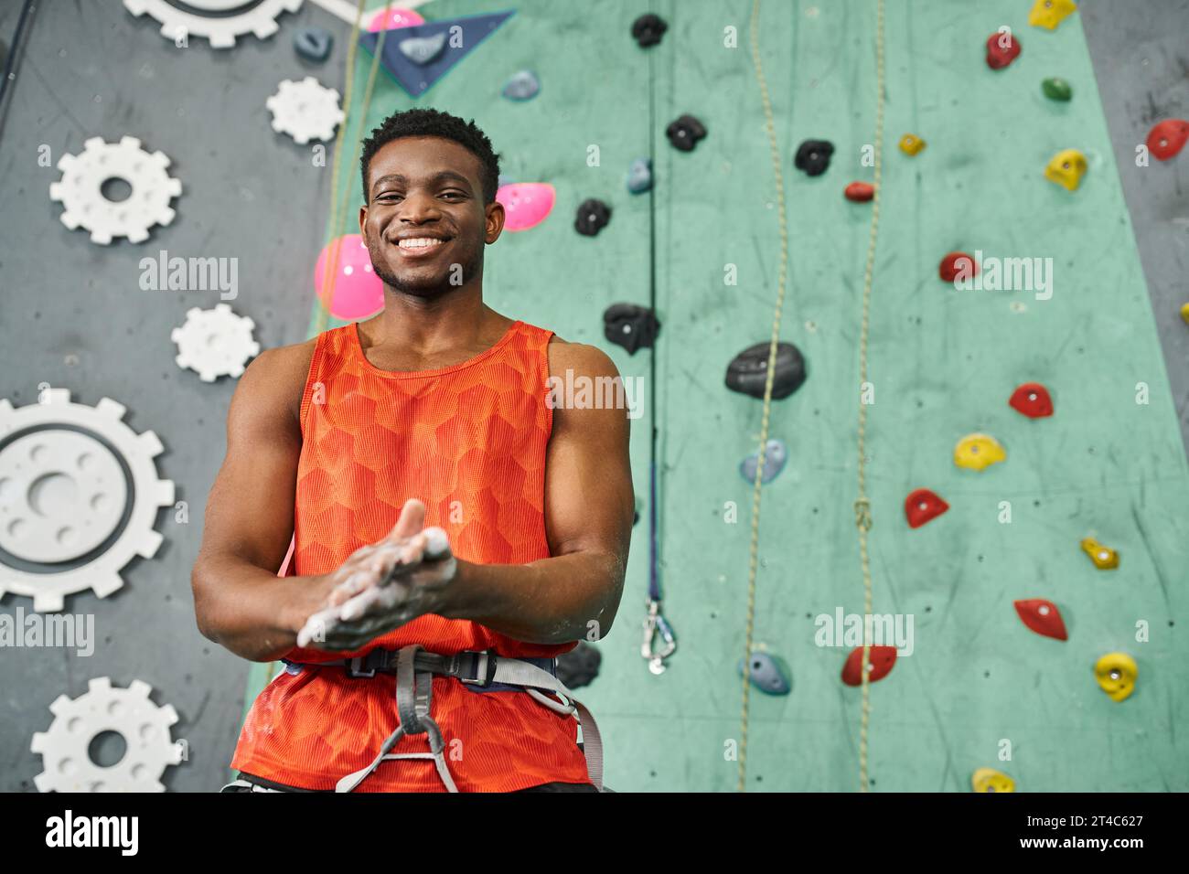 cheerful african american man using talc powder before climbing up wall ...