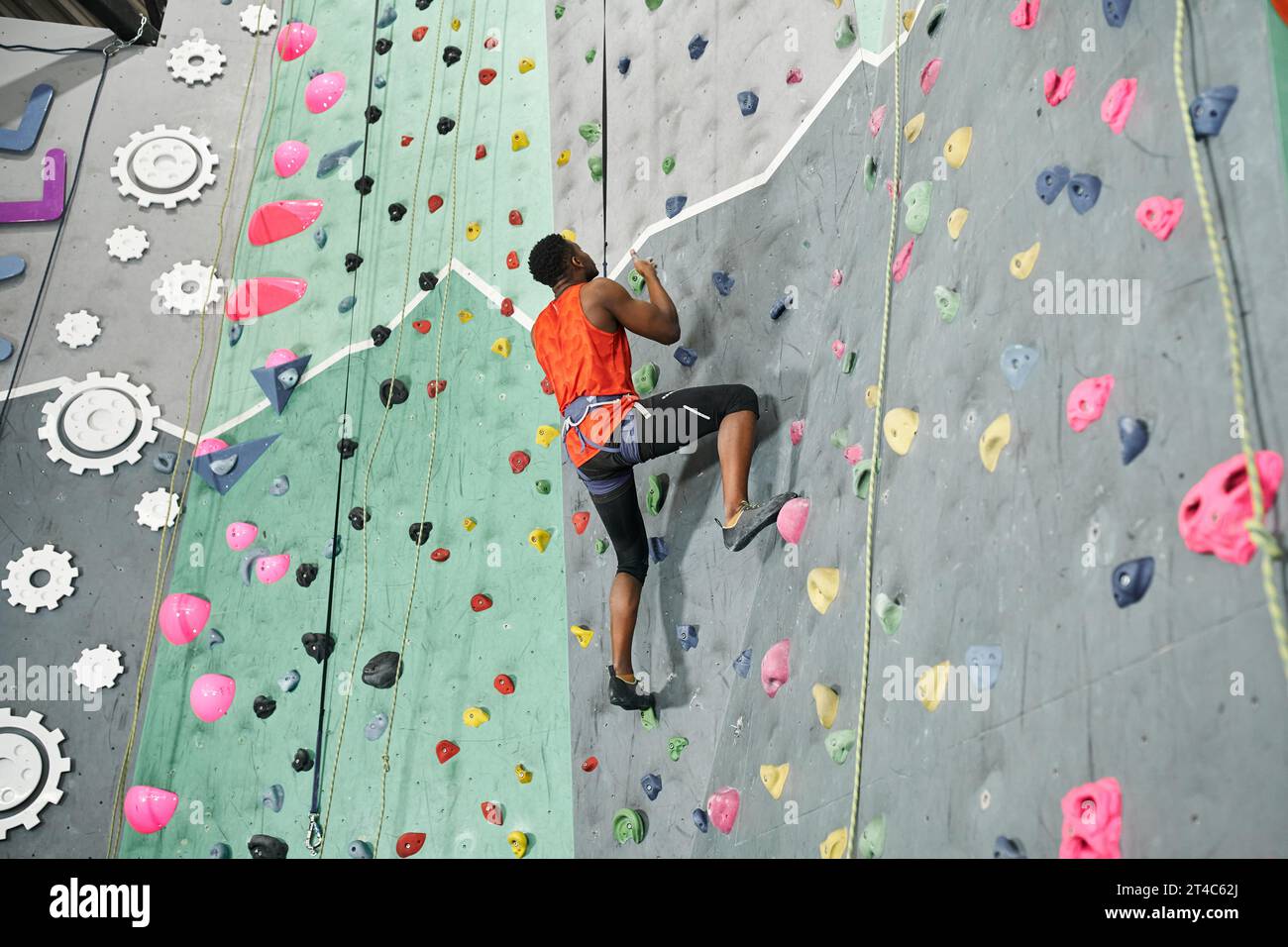 young african american man in orange shirt climbing up rock wall with ...