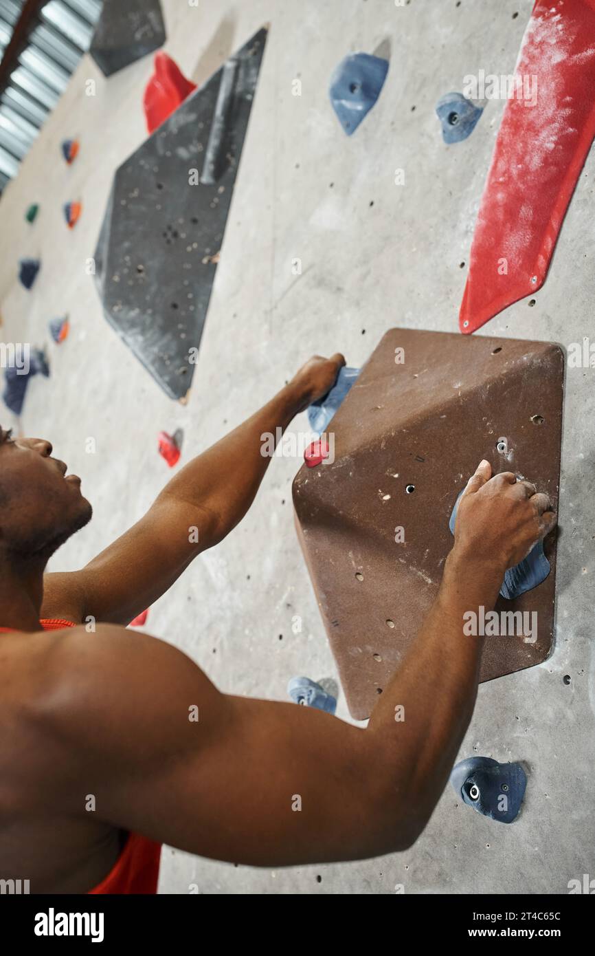 vertical shot of sporty african american man hanging on boulder on ...