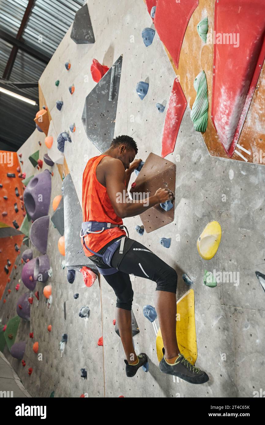 vertical shot of muscular african american man climbing up bouldering ...