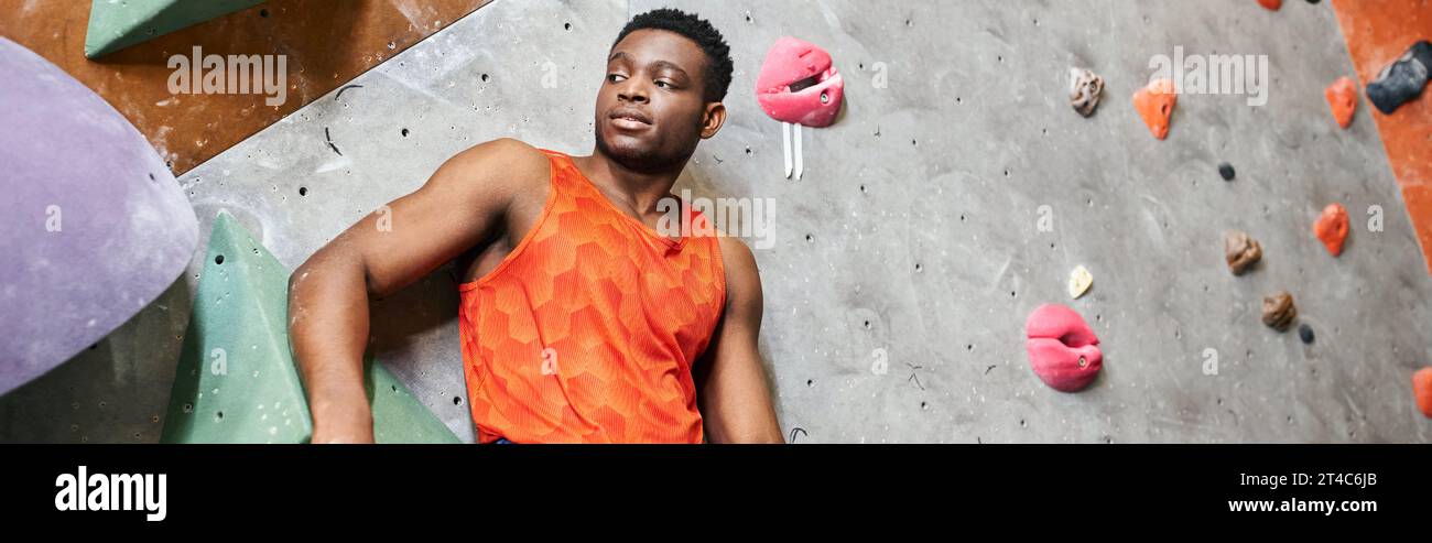sporty african american man standing next to rock climbing wall and ...