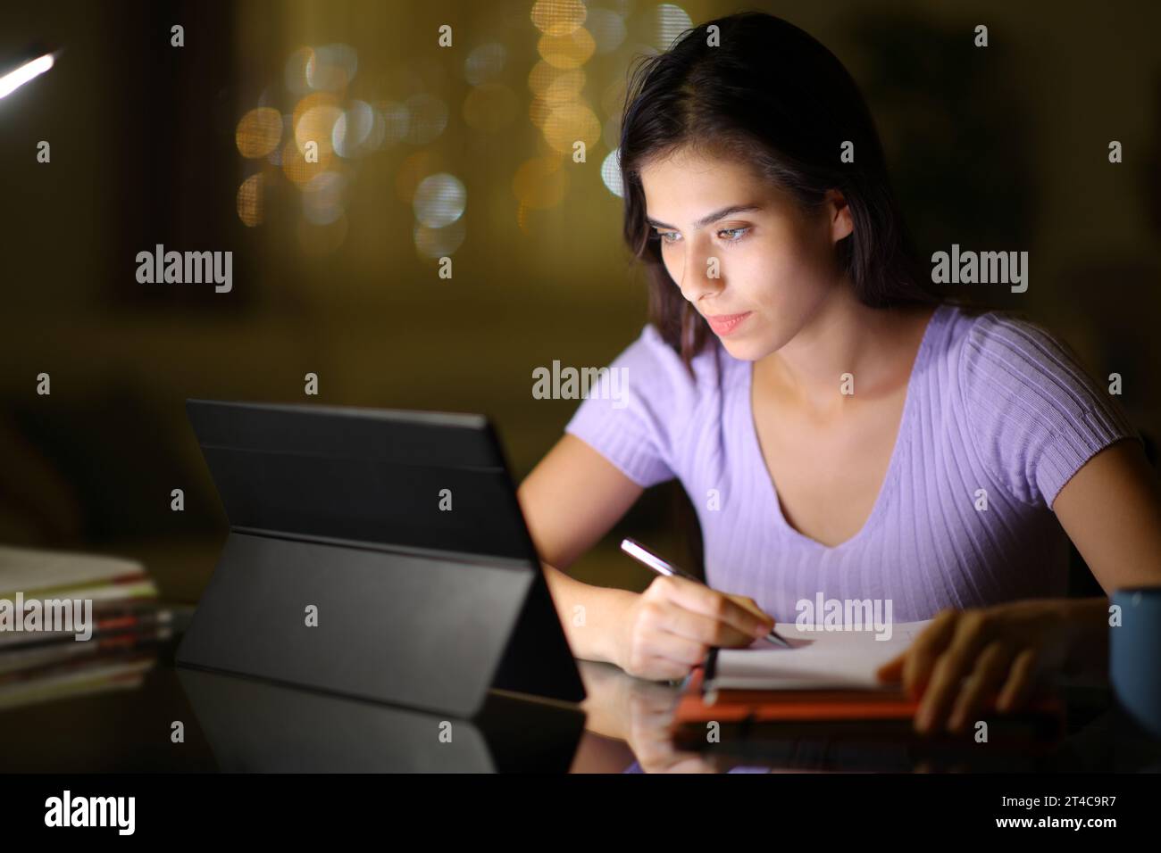 Student e-learning in the night using tablet and taking notes at home ...