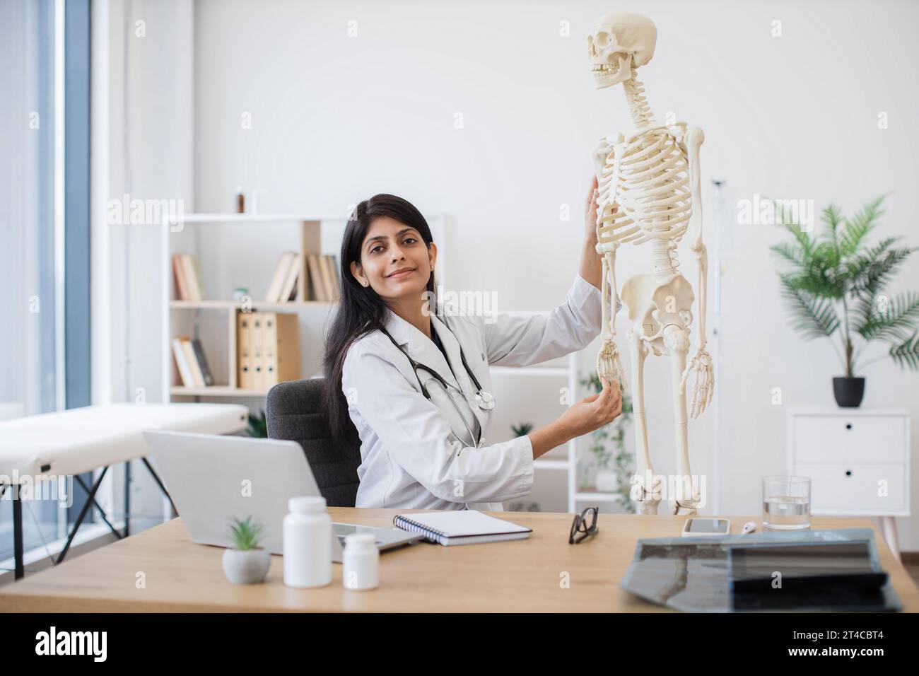 Indian female practitioner sitting at table with modern laptop and ...