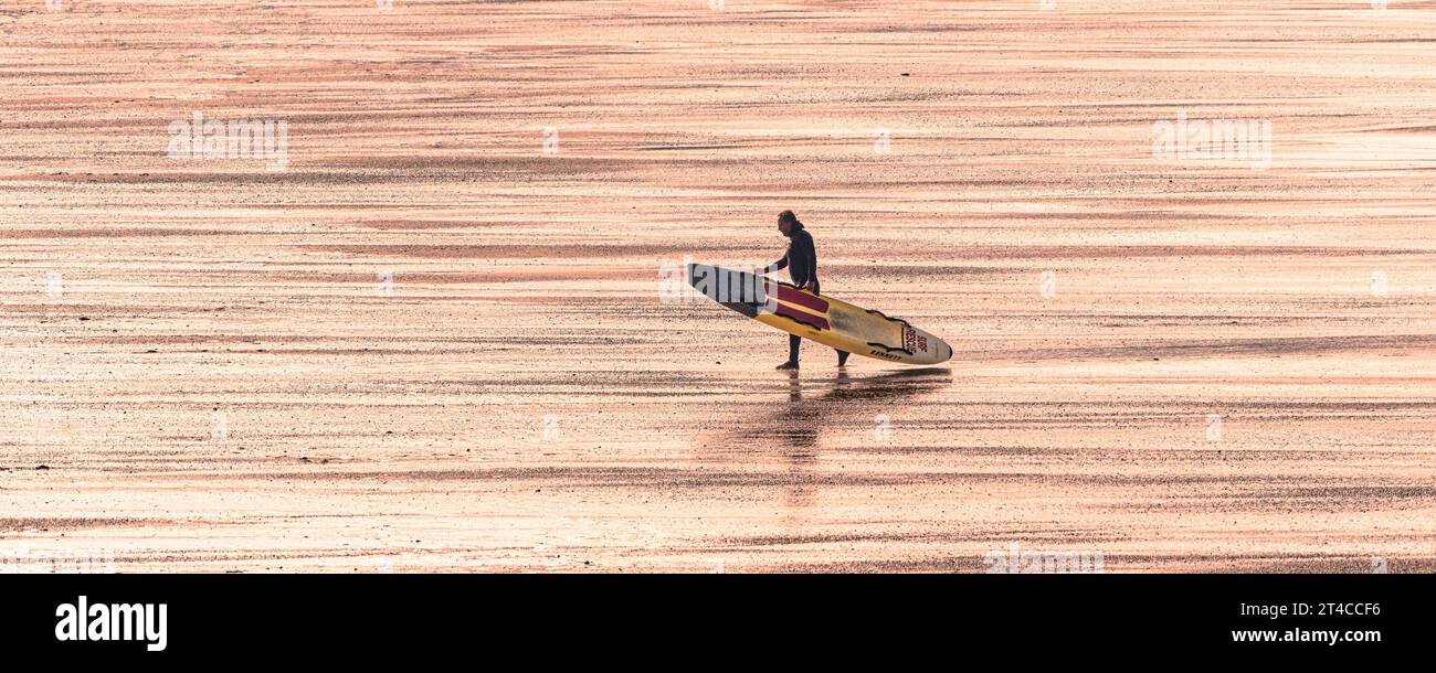 A panoramic image of evening light over a tired mature surfer dragging ...