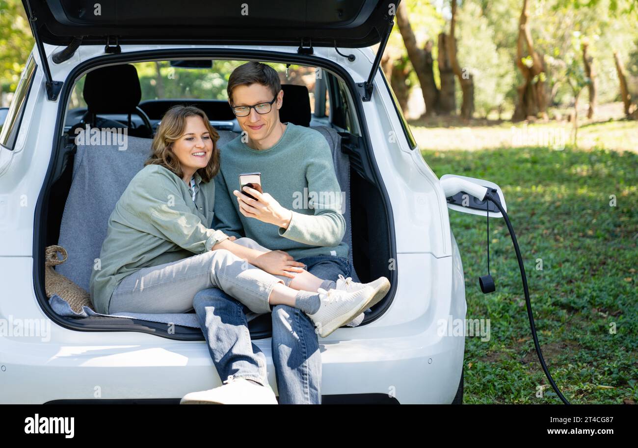 Loving couple with smartphones sits in an electric car's trunk Stock ...