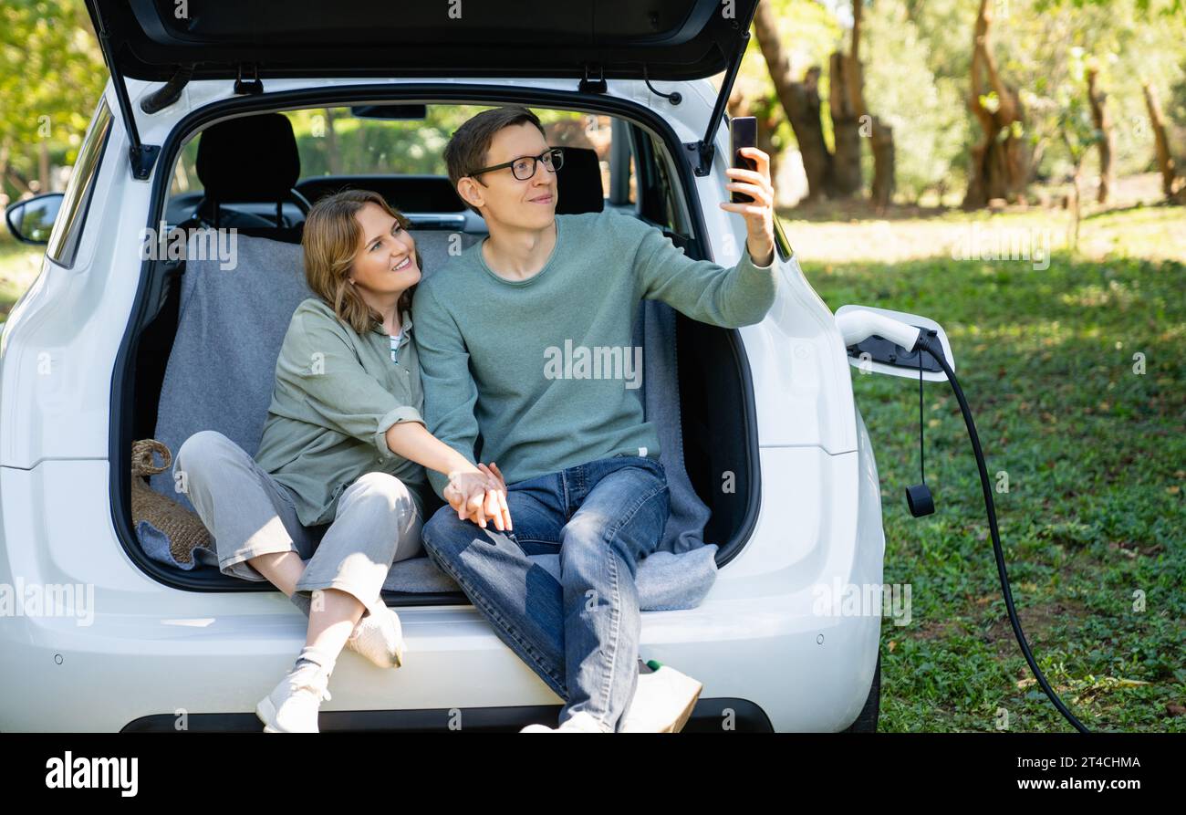 Loving couple with smartphones sits in an electric car's trunk Stock ...