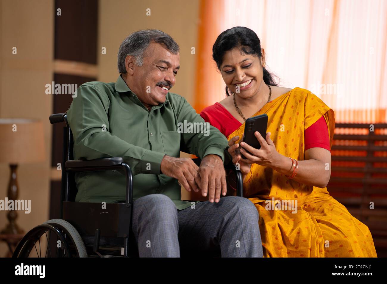 Sick or injured laughing Senior husband on wheelchair watching mobile ...