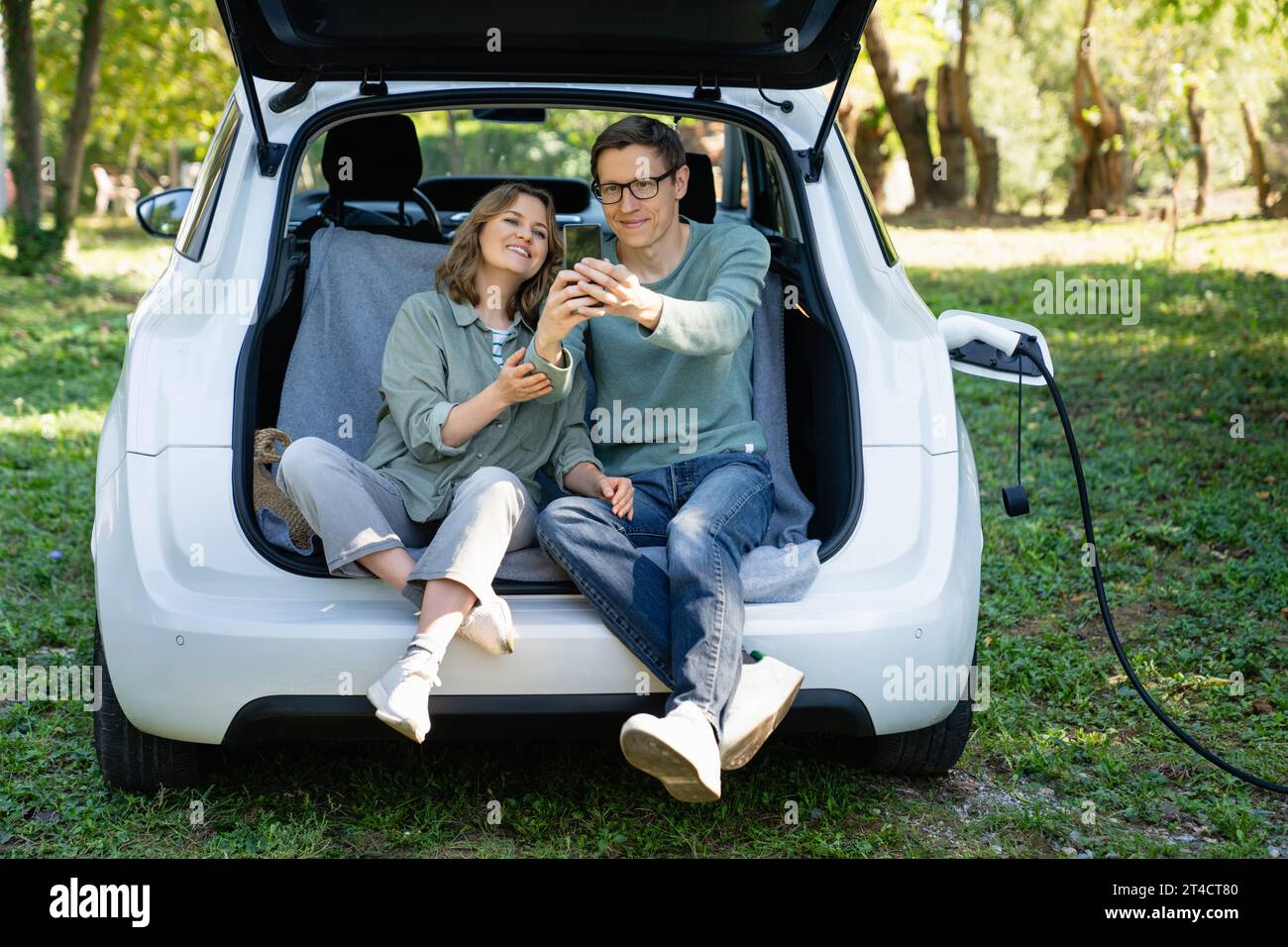 Loving couple with smartphones sits in an electric car's trunk Stock ...