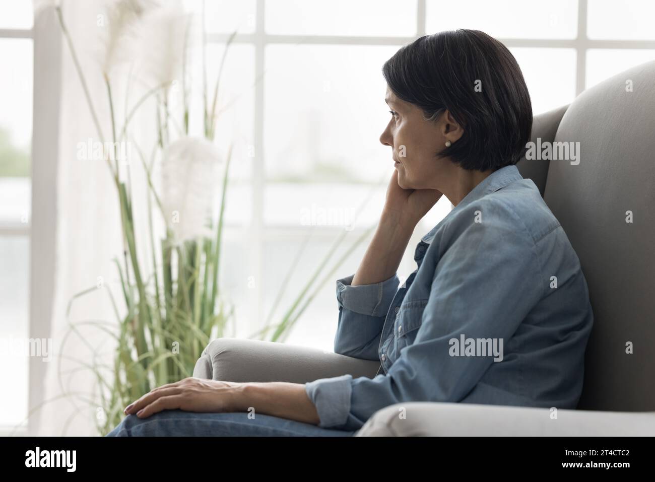 Pensive mature woman sits on armchair staring into distance Stock Photo ...