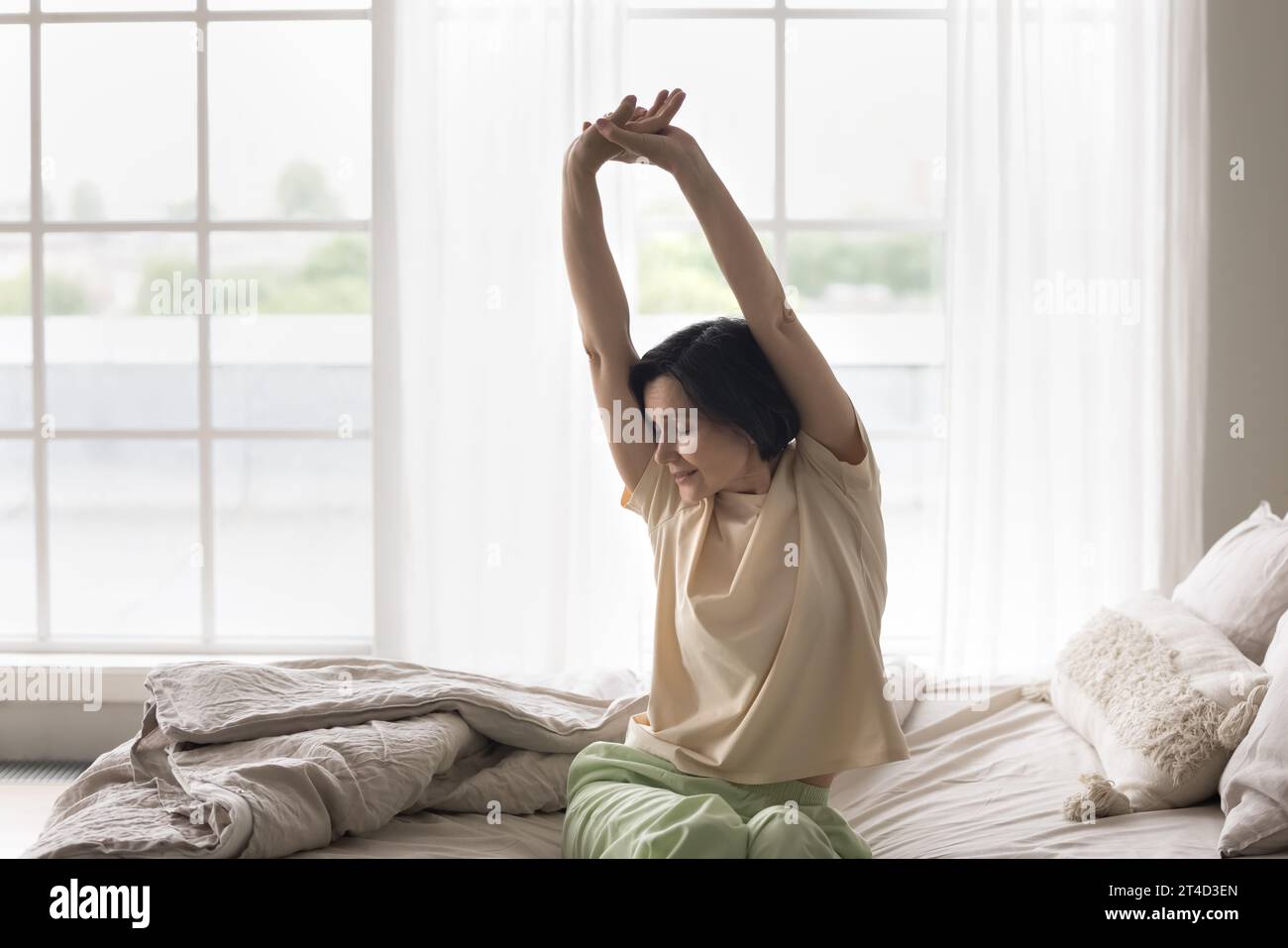 Mature woman waking up, stretching her body seated in bed Stock Photo ...