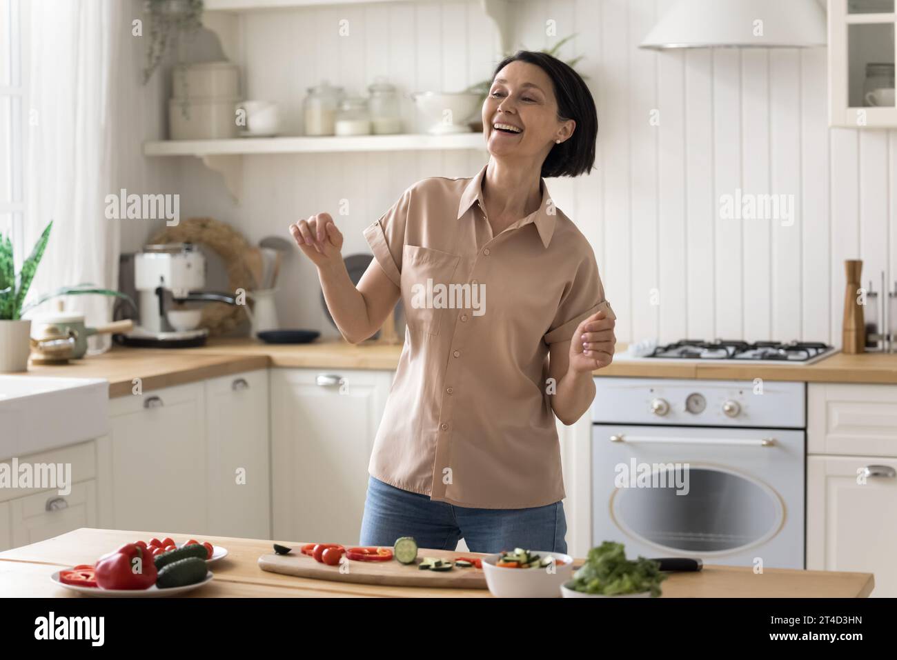 Lively middle-aged female cooking, dancing in modern kitchen Stock ...