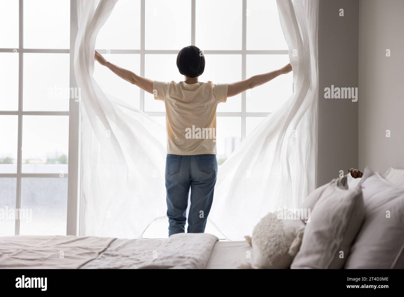 Rear view mature woman opening curtains in the morning Stock Photo - Alamy