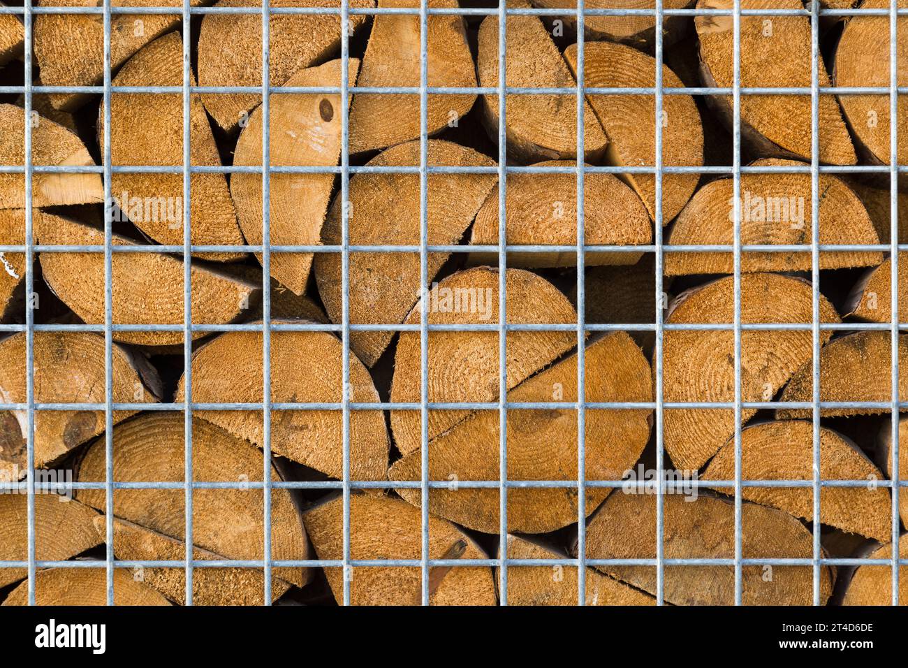 Wooden firewood logs are stacked behind a metal mesh. Wood texture and ...