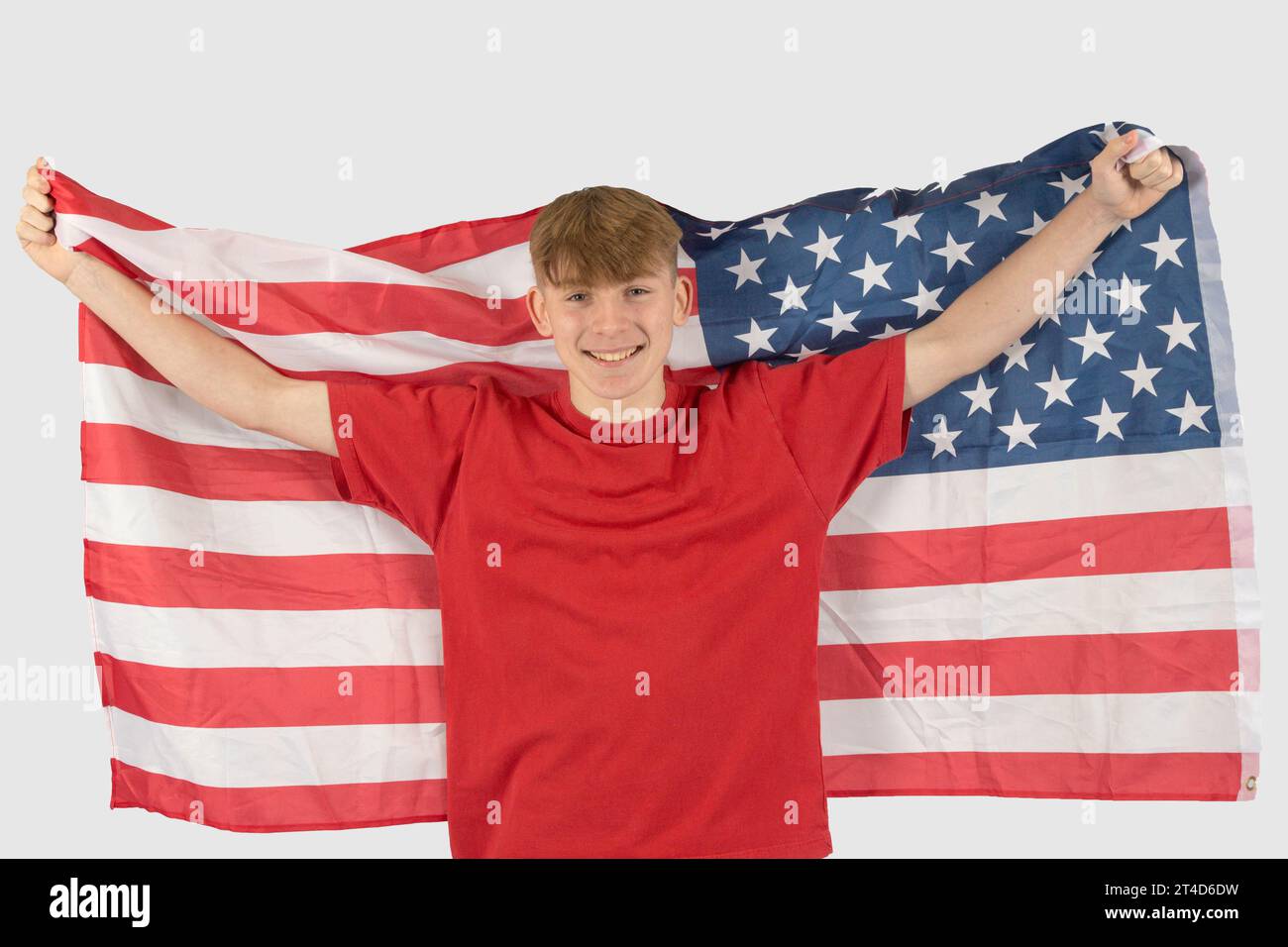 Caucasian teenage boy wearing a red t-shirt holding the American Flag ...