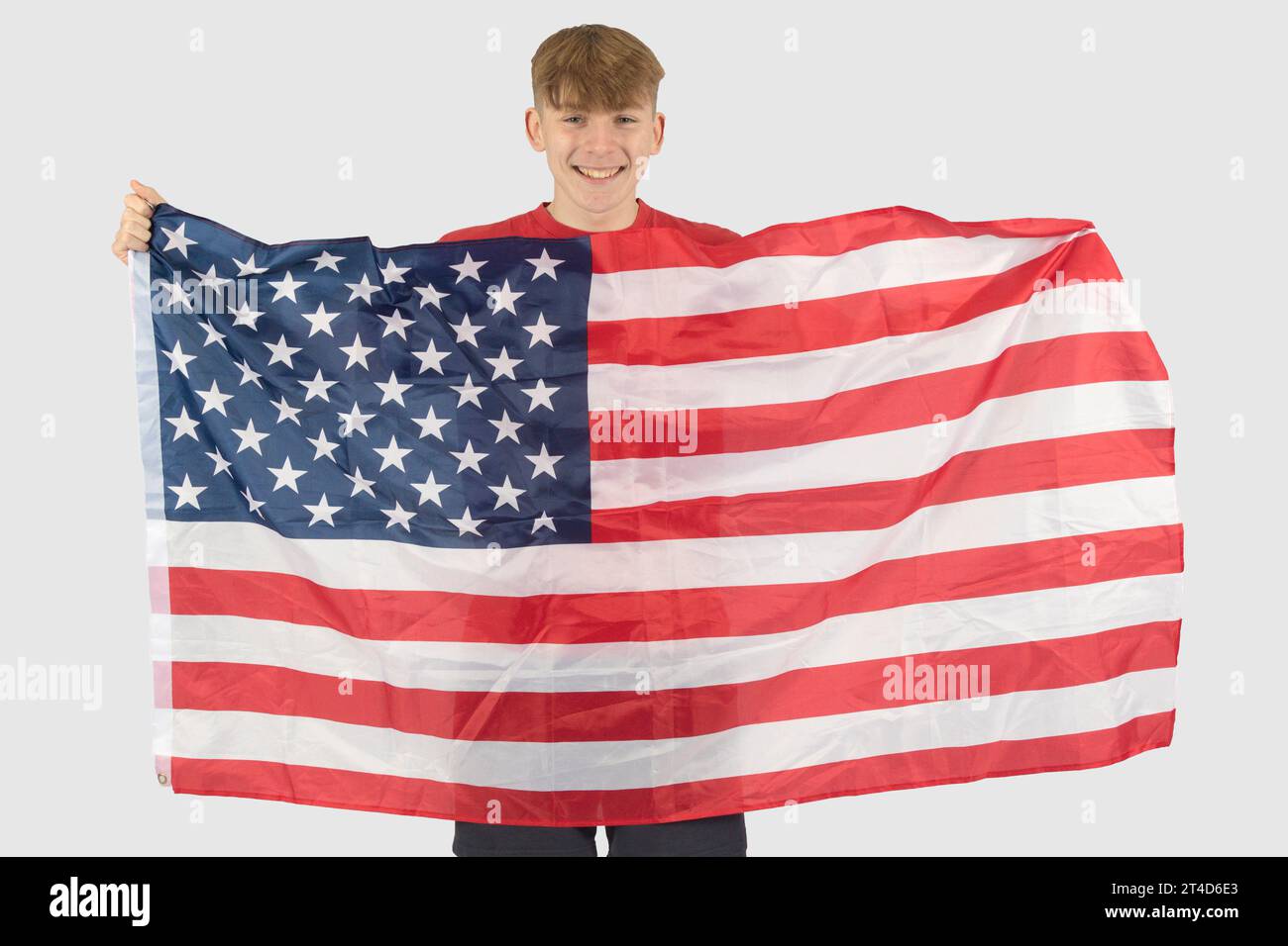 Caucasian teenage boy wearing a red t-shirt holding the American Flag ...