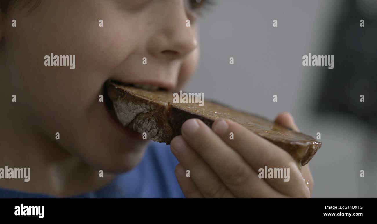 One small boy taking a bite of toast bread, close-up child mouth eating ...