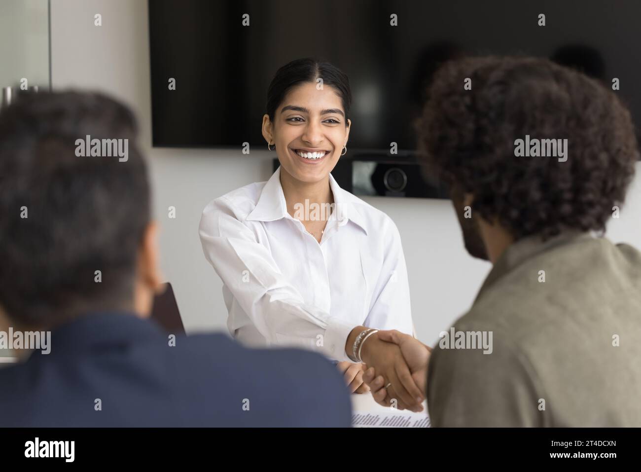 Happy pretty young Indian businesswoman giving handshake to business ...