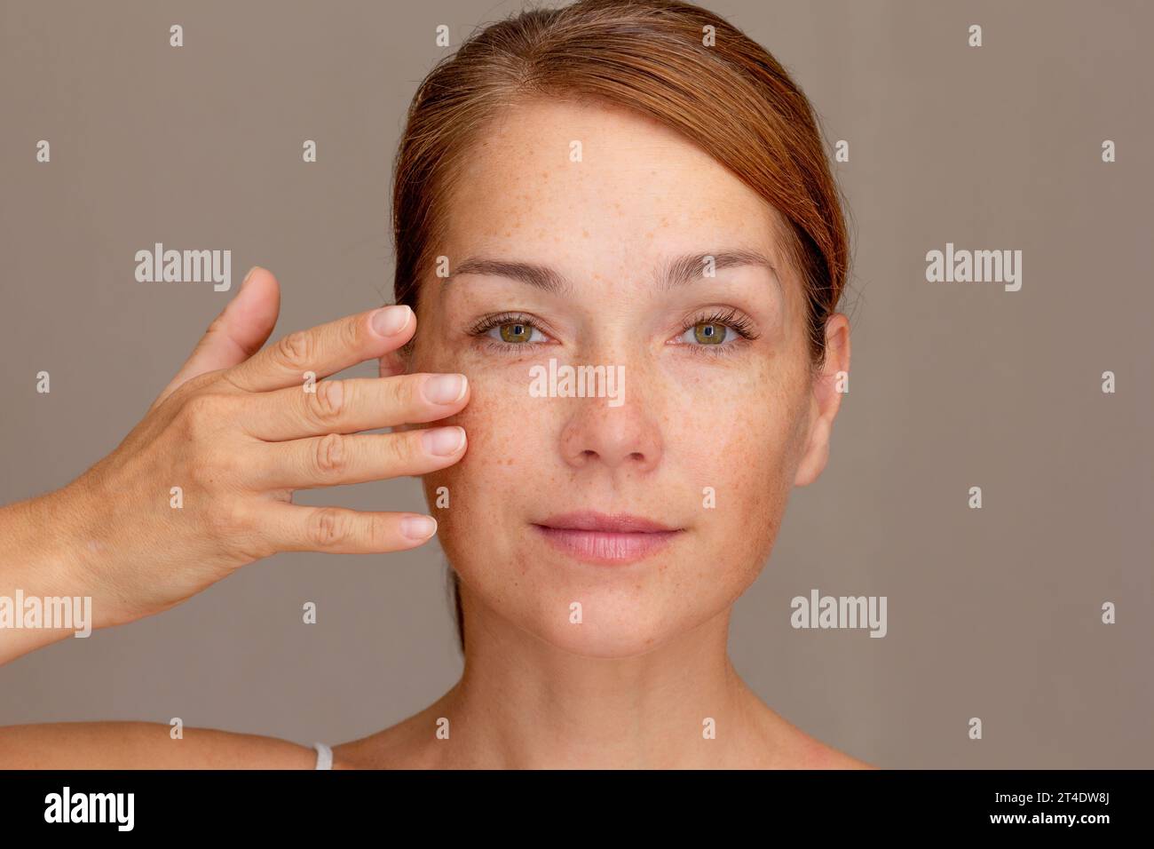 Portrait of cropped caucasian middle aged woman face with freckles holding fingers on cheek ...