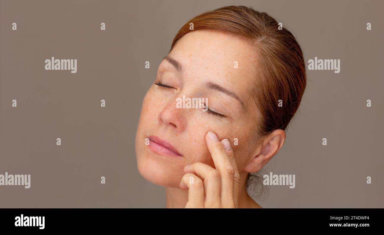 Portrait of cropped caucasian middle aged woman face with freckles holding fingers on cheek ...