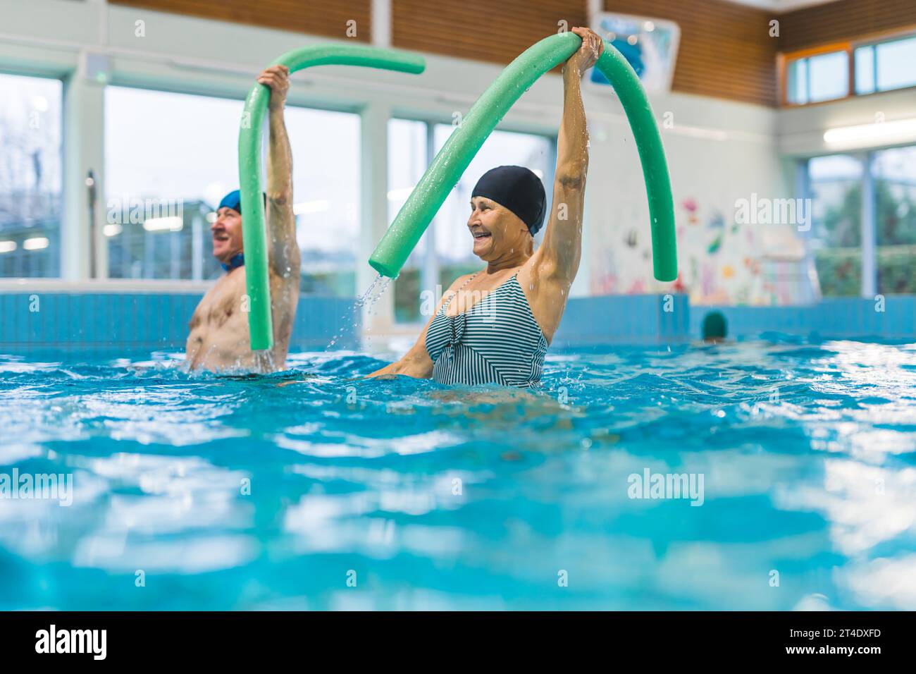 Older adults man and woman doing aquatic exercises with water noodles ...