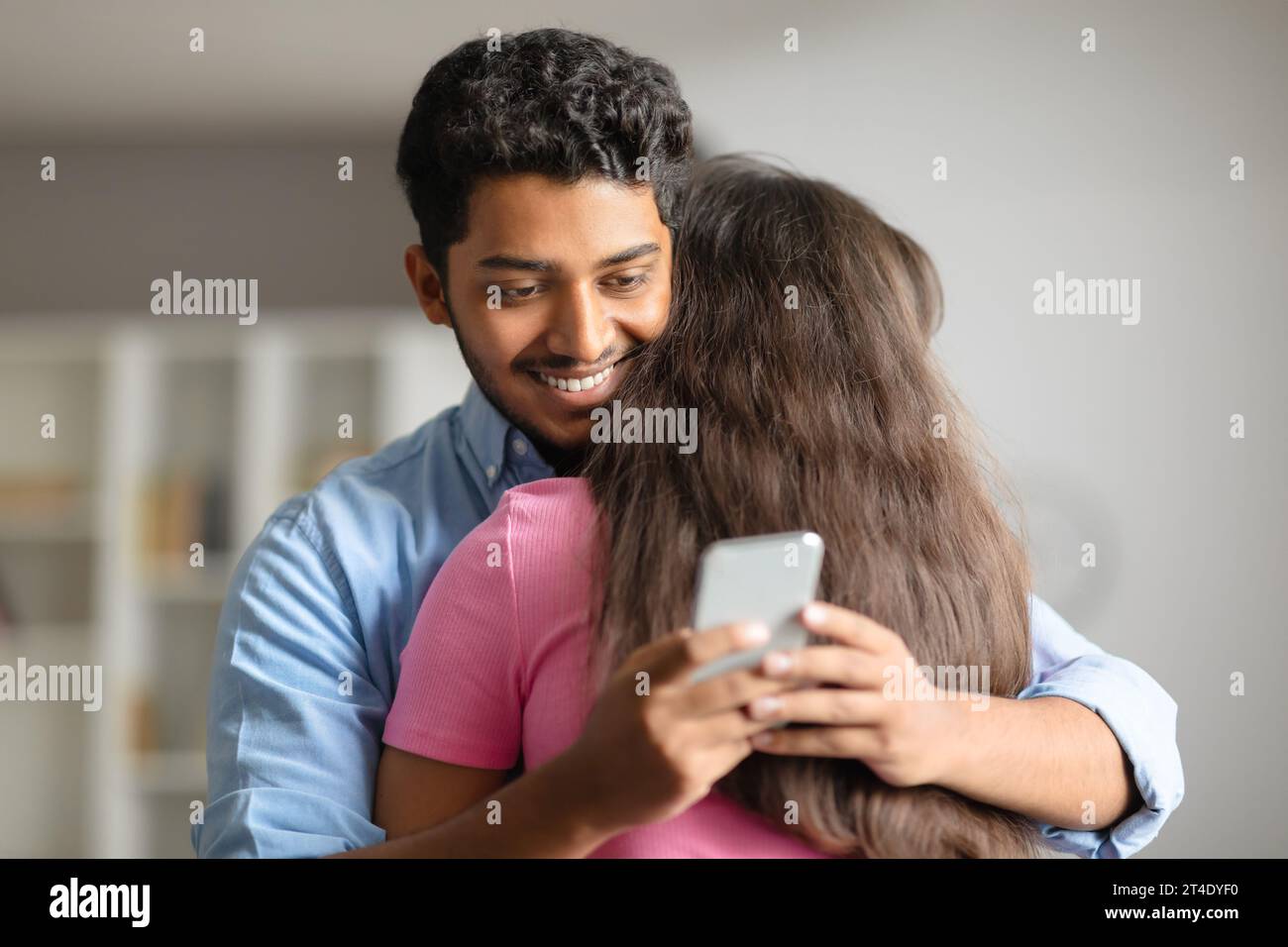 Indian man hugs wife, using phone secretly Stock Photo - Alamy