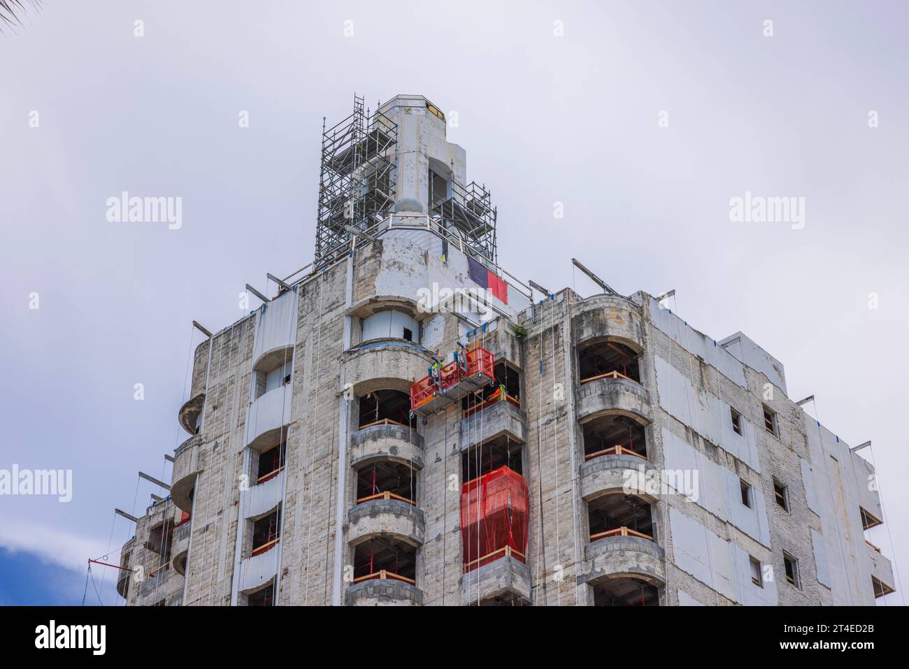 Top of tall building partially covered in construction nets, undergoing ...